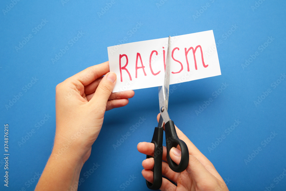 Hand holding card with the text racism. Top view of black scissors and ...