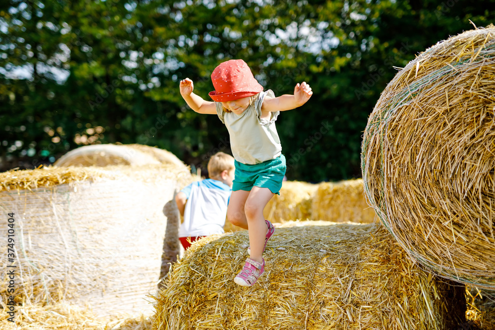 Little toddler girl having fun with running and jumping on hay stack or ...