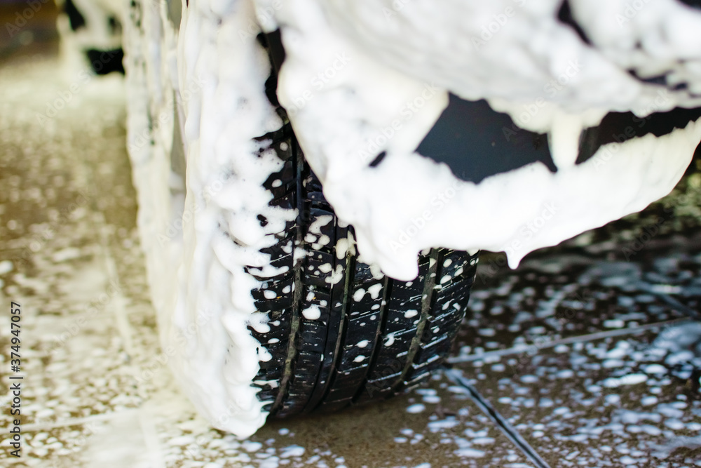 The wheel of a car, covered in soapy foam at a car wash station ...