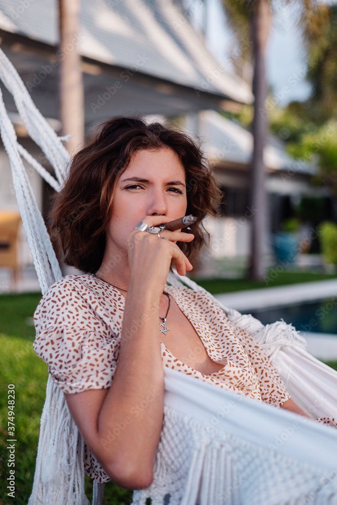 Young european woman smoking cigar lying on hammock outside tropical ...