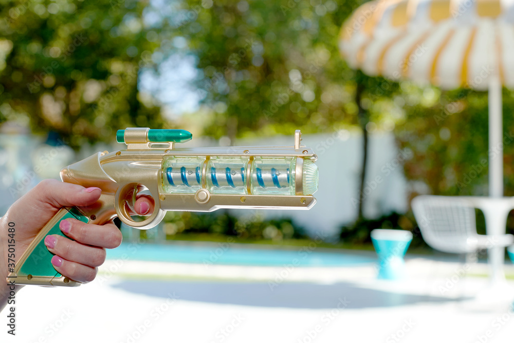 Female hand holding a toy water gun by the pool in the backyard. foto ...