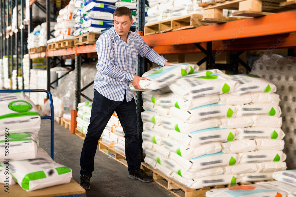Glad smiling Man choosing compost soil in plastic bags in hypermarket ...
