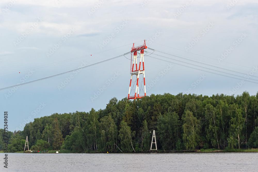 Red-white High voltage tower over the water. Electricity pylon,cables ...