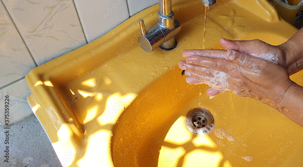 washing of both hands with soap under a yellow wash basin with running ...