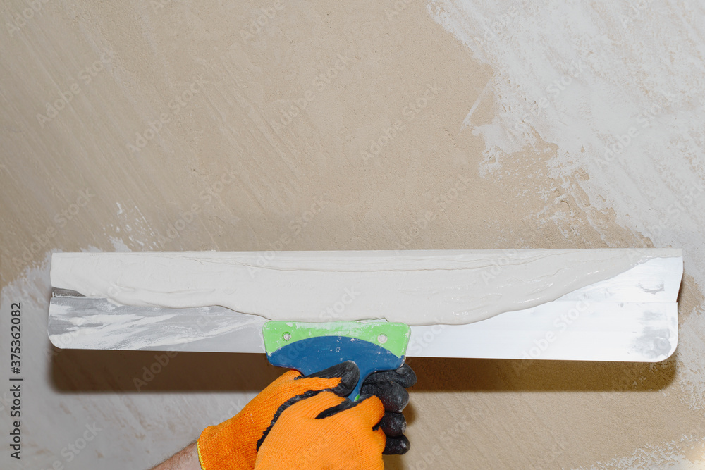 hand with a long trowel with white putty on a plaster background Stock ...