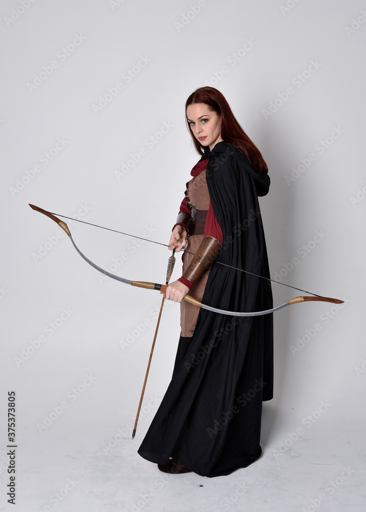 Full length portrait of girl with red hair wearing medieval archer ...