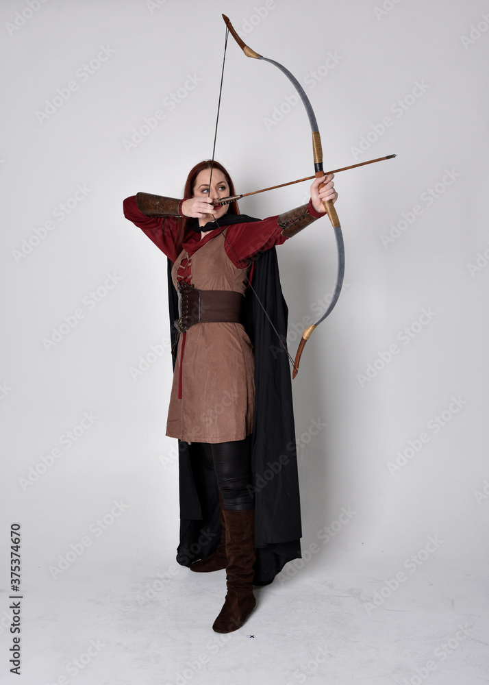 Full length portrait of girl with red hair wearing medieval archer ...