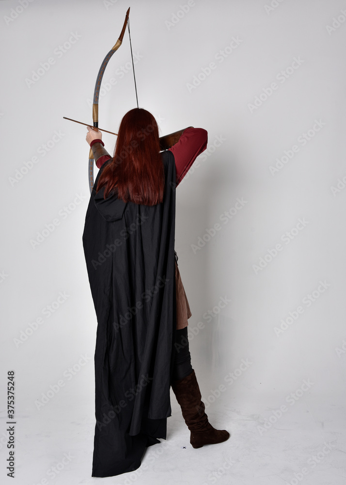 Full length portrait of girl with red hair wearing medieval archer ...