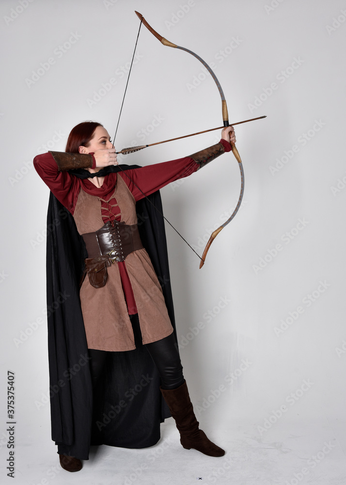 Full length portrait of girl with red hair wearing medieval archer ...