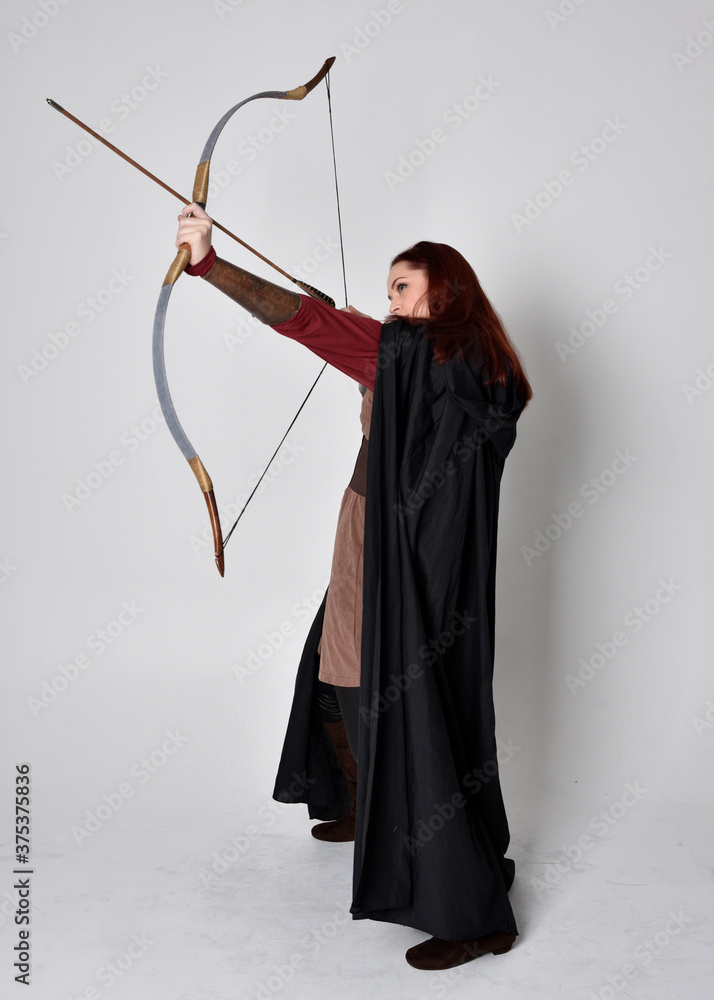 Full length portrait of girl with red hair wearing medieval archer ...