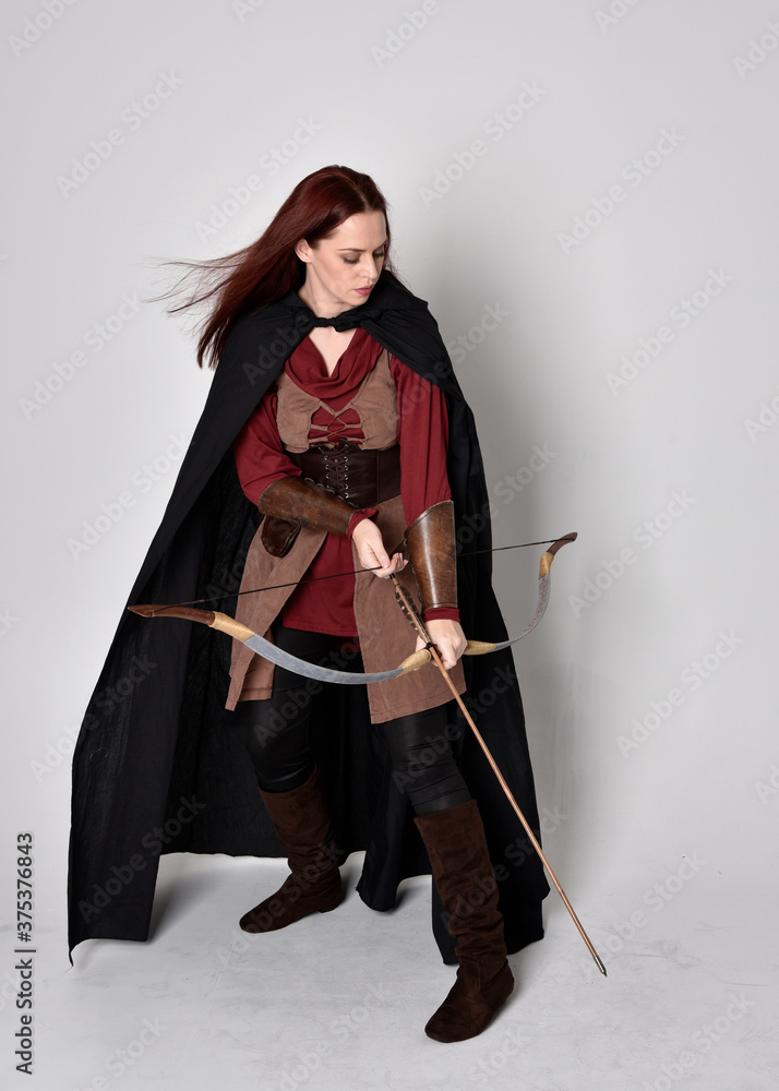 Full length portrait of girl with red hair wearing medieval archer ...