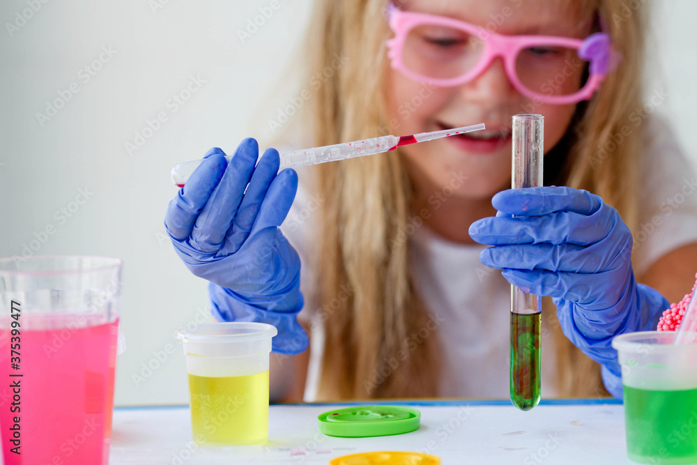A little girl in pink glasses conducts experiments. A child in rubber ...