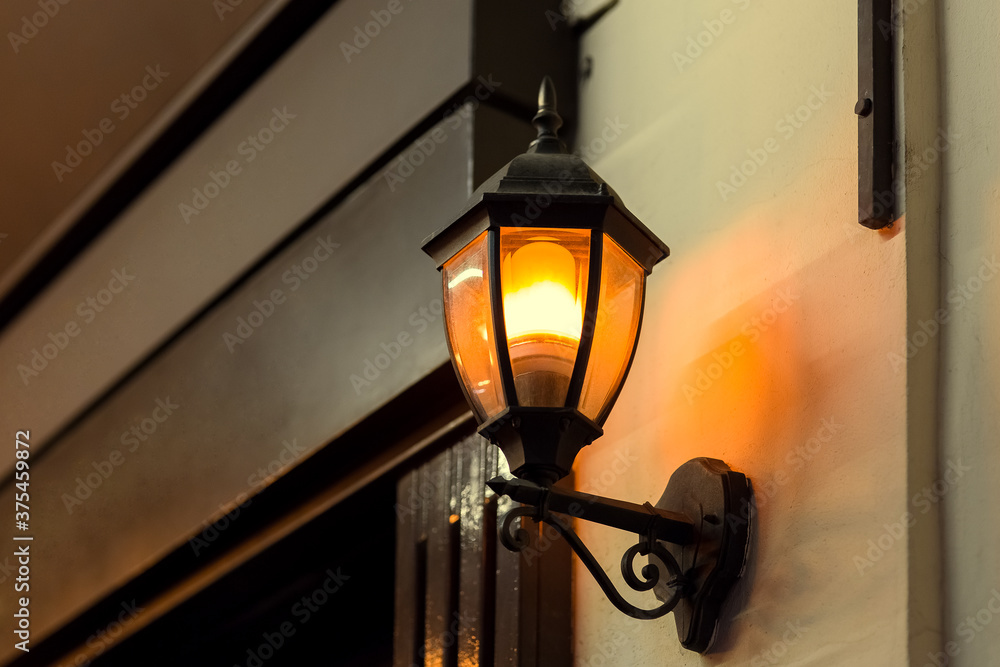 black iron lantern in retro style illuminates wall of building facade ...