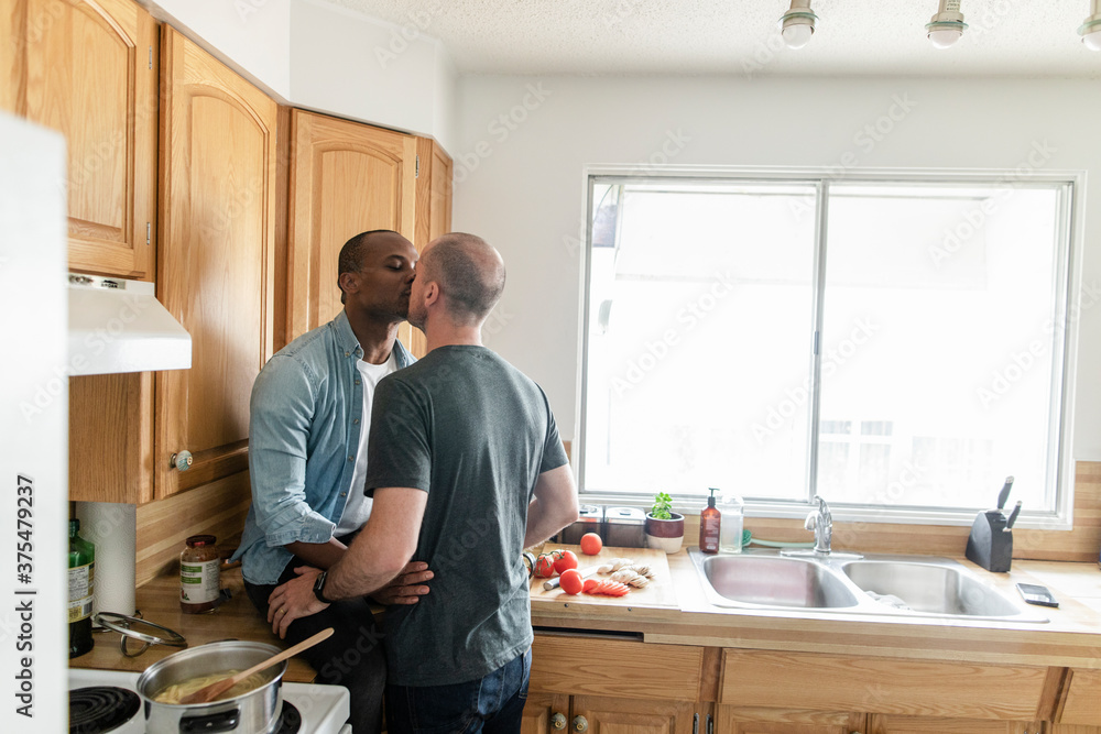 Multiethnic gay male couple kissing and cooking in kitchen Stock Photo ...