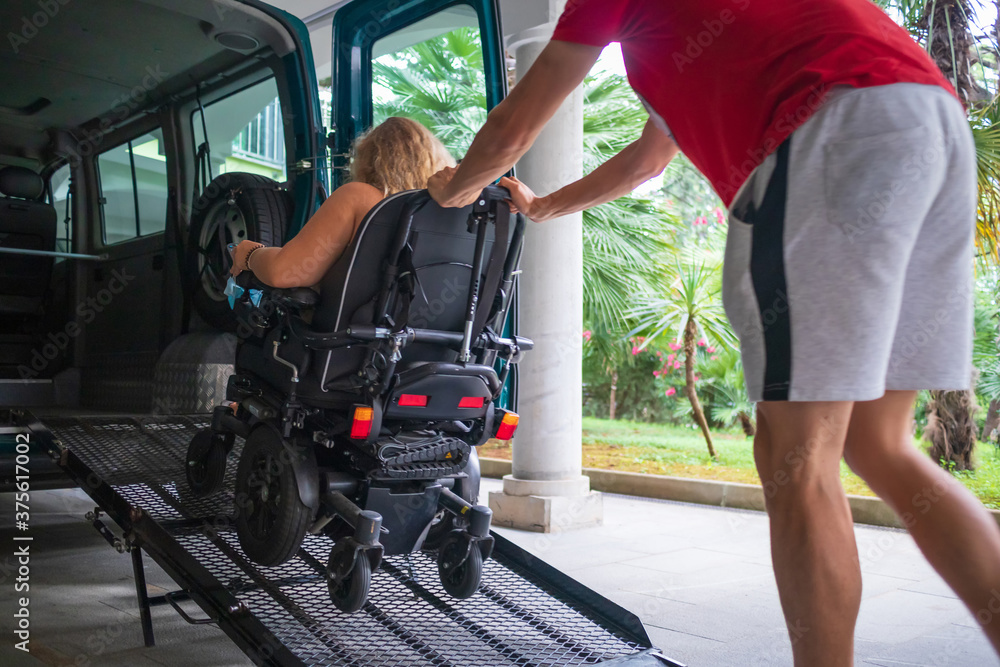 Driver assisting disabled person on wheelchair with transport using ...