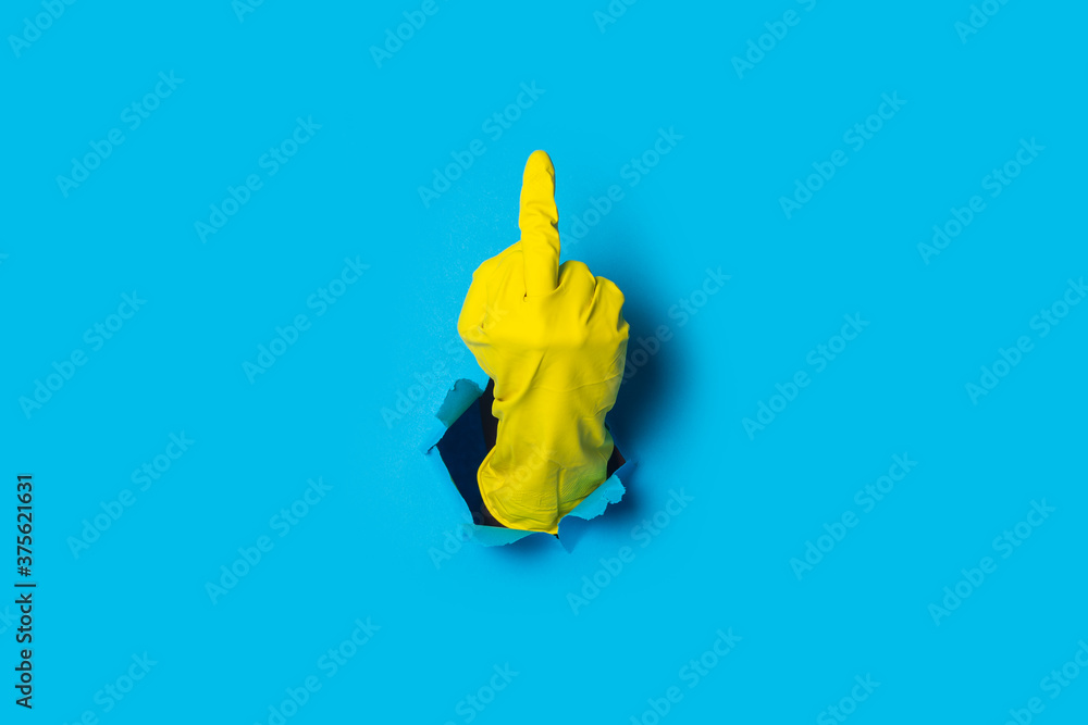 Hand in yellow glove showing middle finger on a bright blue background ...