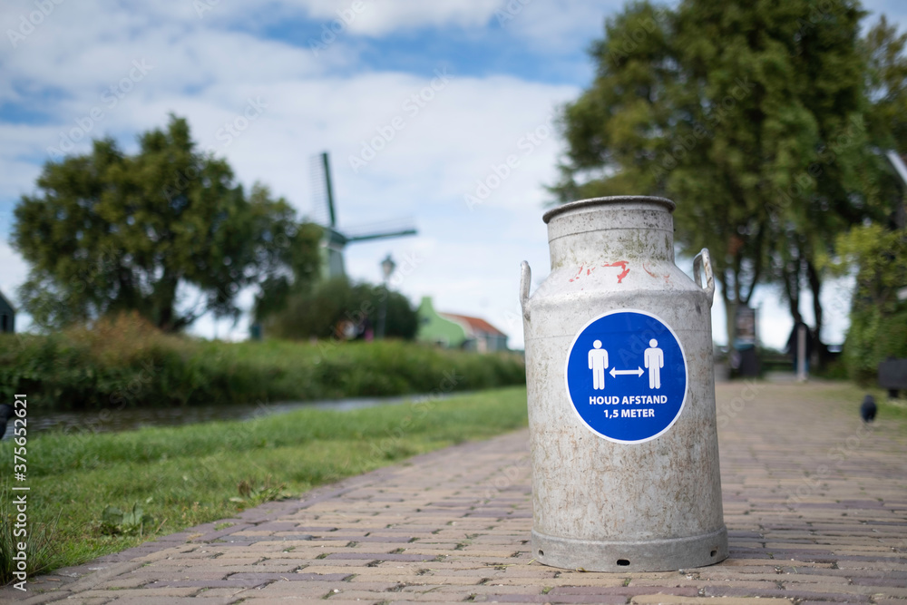 Milk can on a foothpath with blue social distancing sign HOUD AFSTAND ...