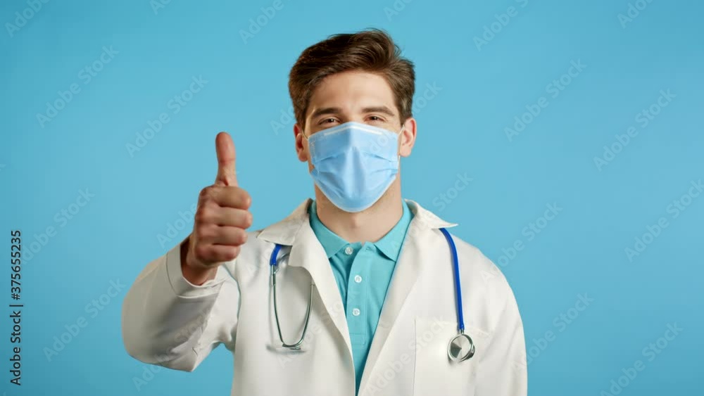Man in medical white coat and mask showing thumb up sign over blue ...