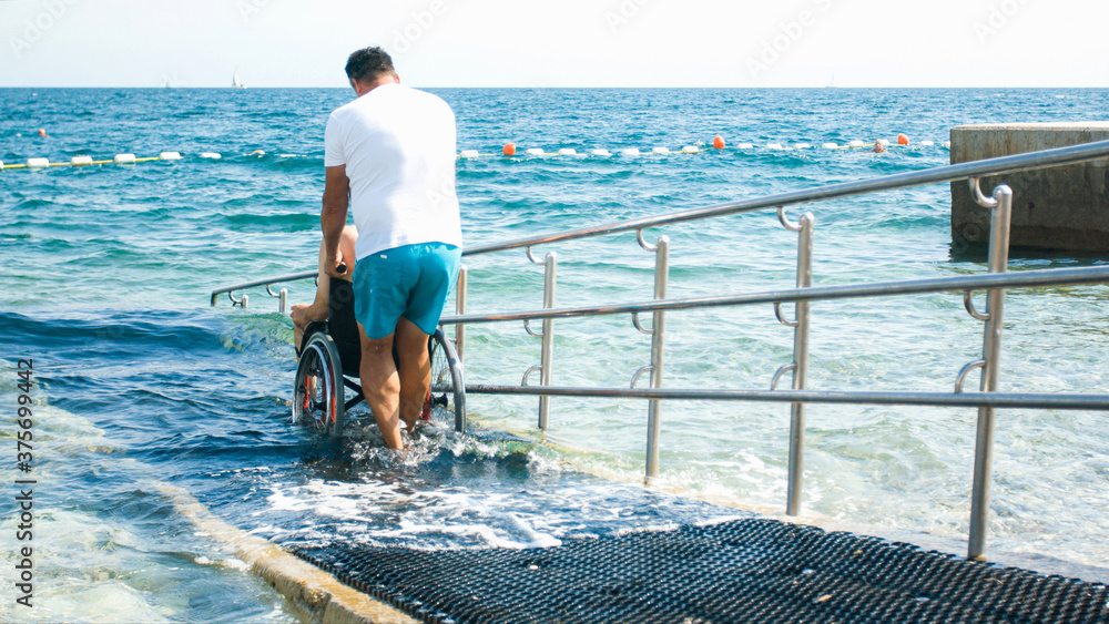 Disabled man at beach swimming on a wheelchair with assistance help on ...