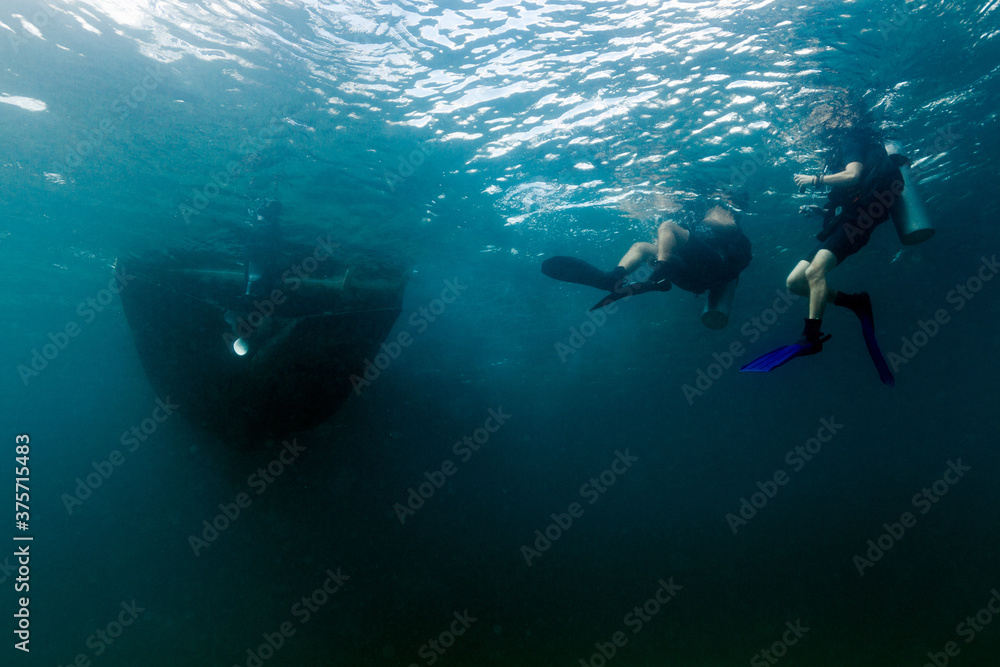 Scuba diver buddies in the sea at the surface next to a boat seen from ...