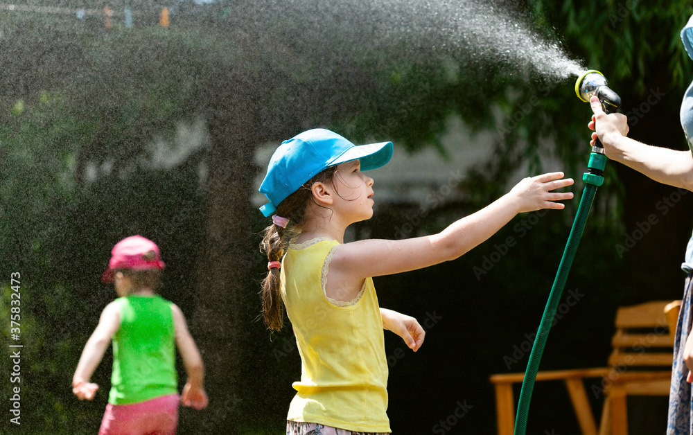 Children playing with water hose in the garden, mother spraying water ...