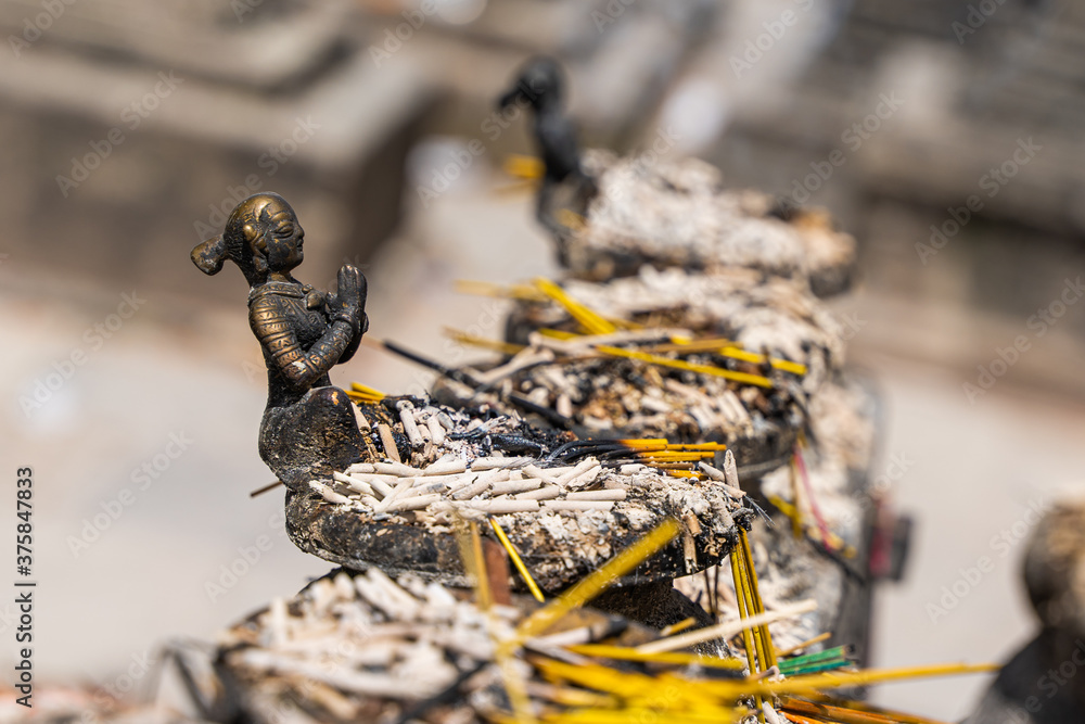 Small praying human figures with a lot of incense sticks around ...