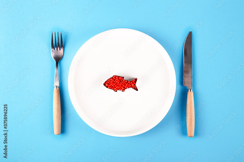 Plastic fish in a plate next to a knife and fork. The concept of ...