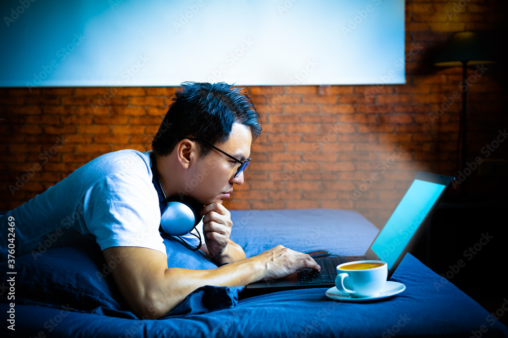 young asian man staring at laptop computer screen in bedroom at night ...