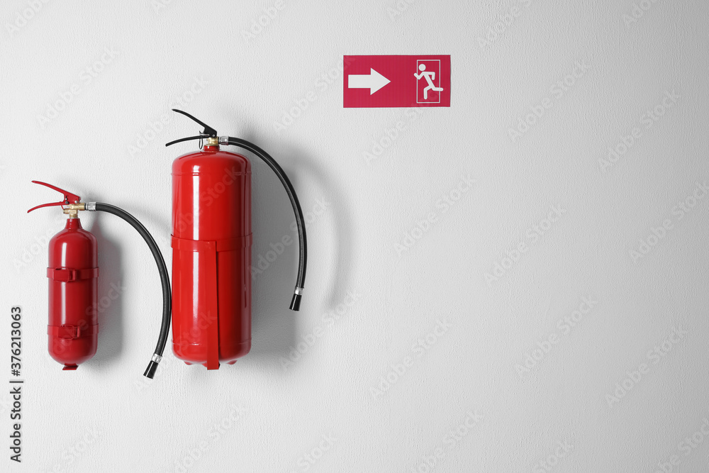 Different fire extinguishers and emergency exit sign on white wall ...