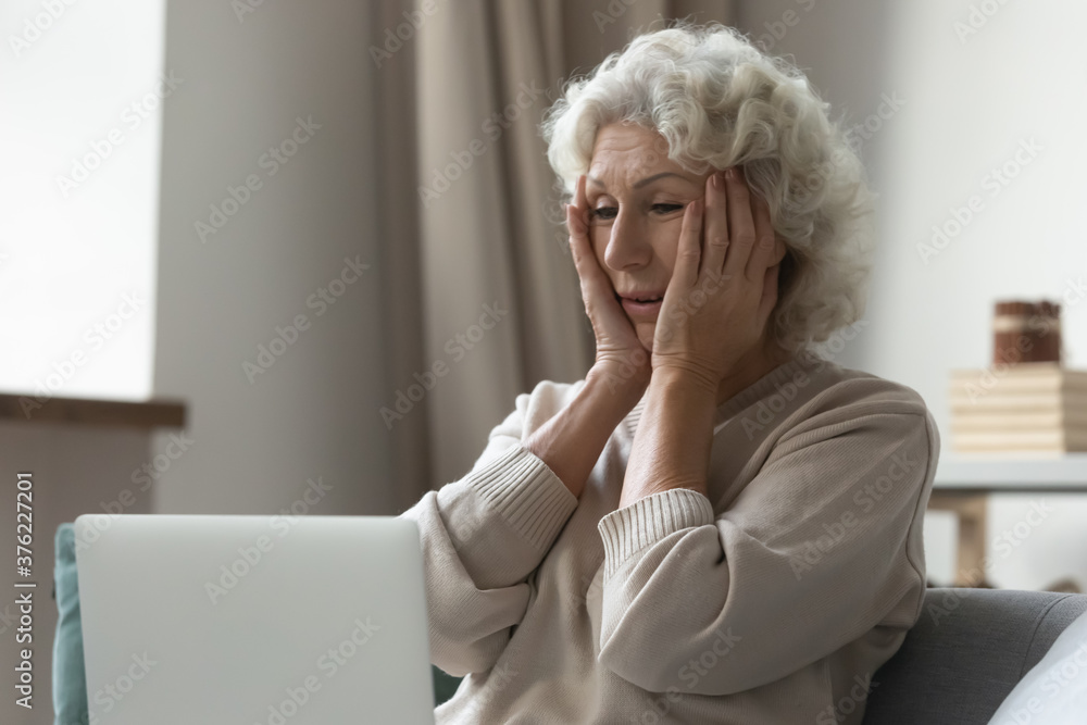 Shocked mature woman looking at laptop screen, touching temples ...