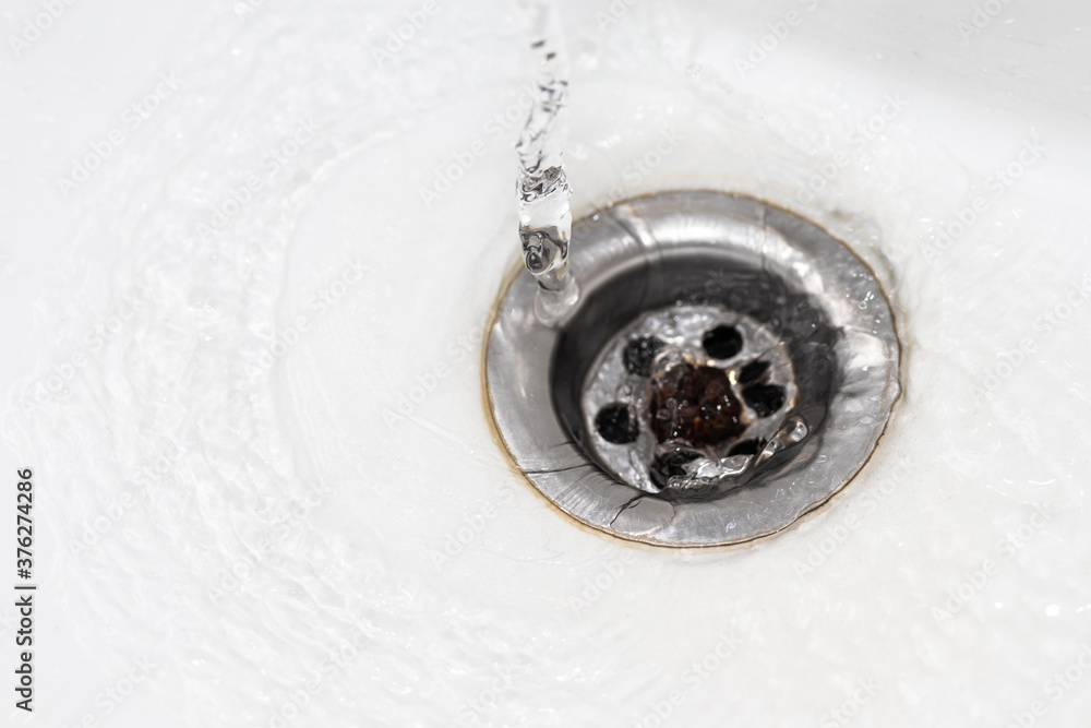 Close up a stream of clean water flows into the sink sewer hole. A jet ...
