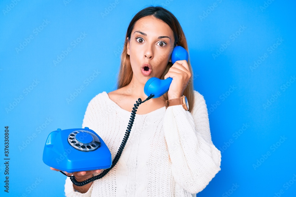 Young brunette woman using vintage telephone scared and amazed with ...