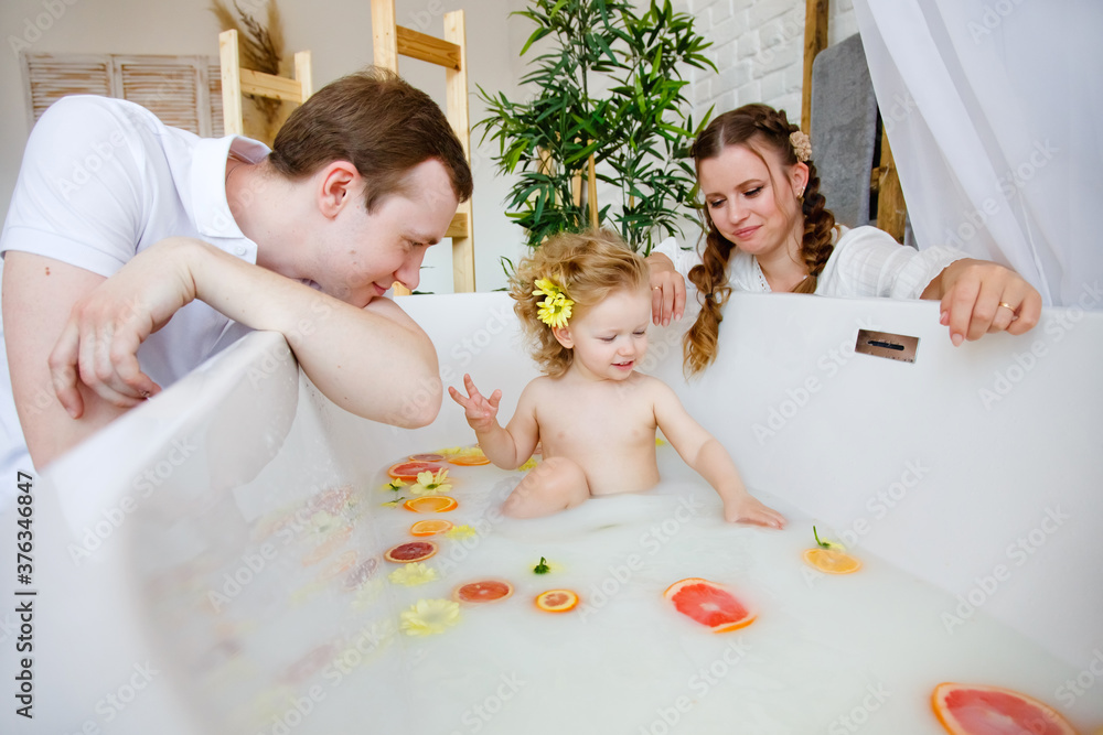Cute little girl sitting in a bath with milk and fruit. A young family ...