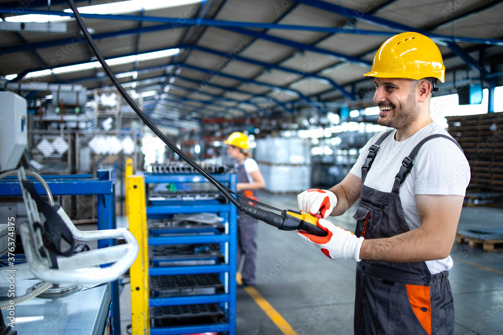 Factory worker wearing uniform and hardhat operating industrial machine ...