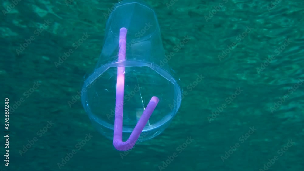 Plastic cocktail cup with a plastic straw slowly drifts underwater in ...