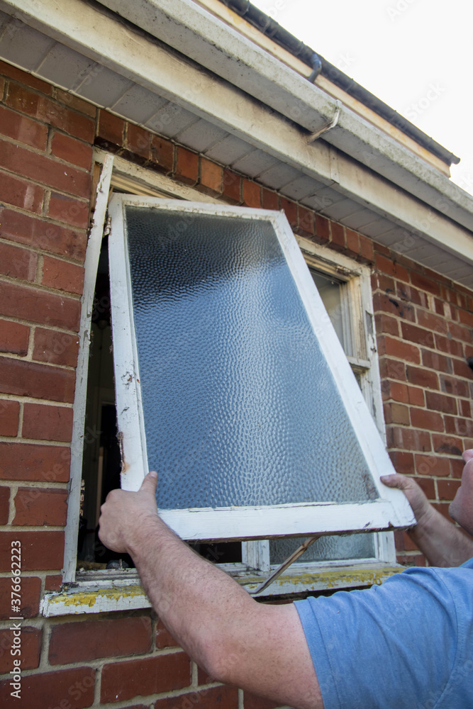 Workman removing old broken window from building during renovation ...