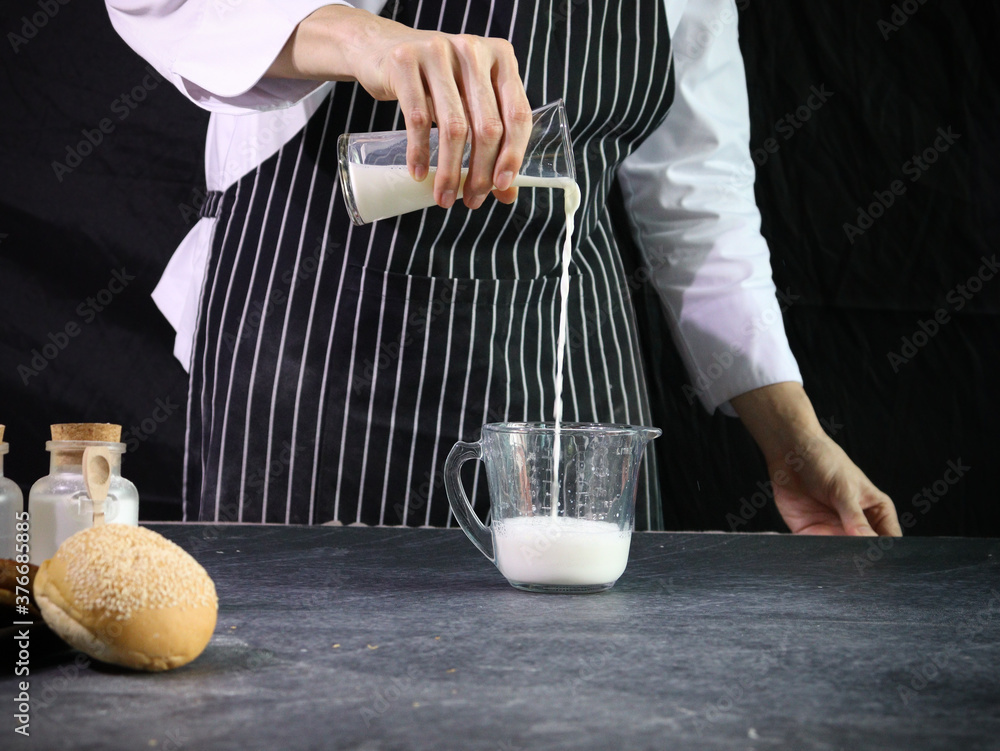 Bakery man pouring milk into a measuring jug in the kitchen at home ...