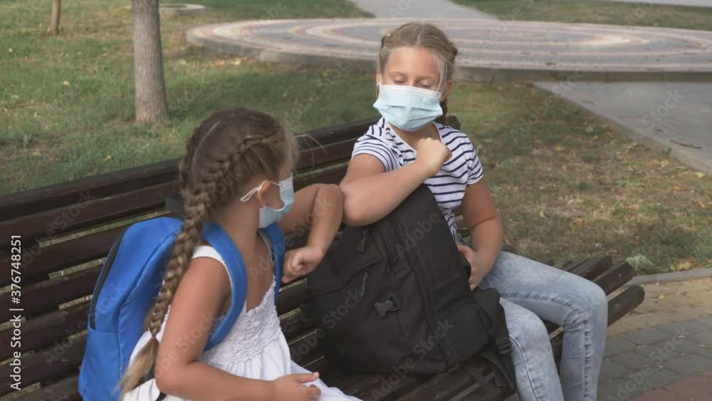 Vidéo Stock Schoolgirls in medical masks are sitting in the park ...
