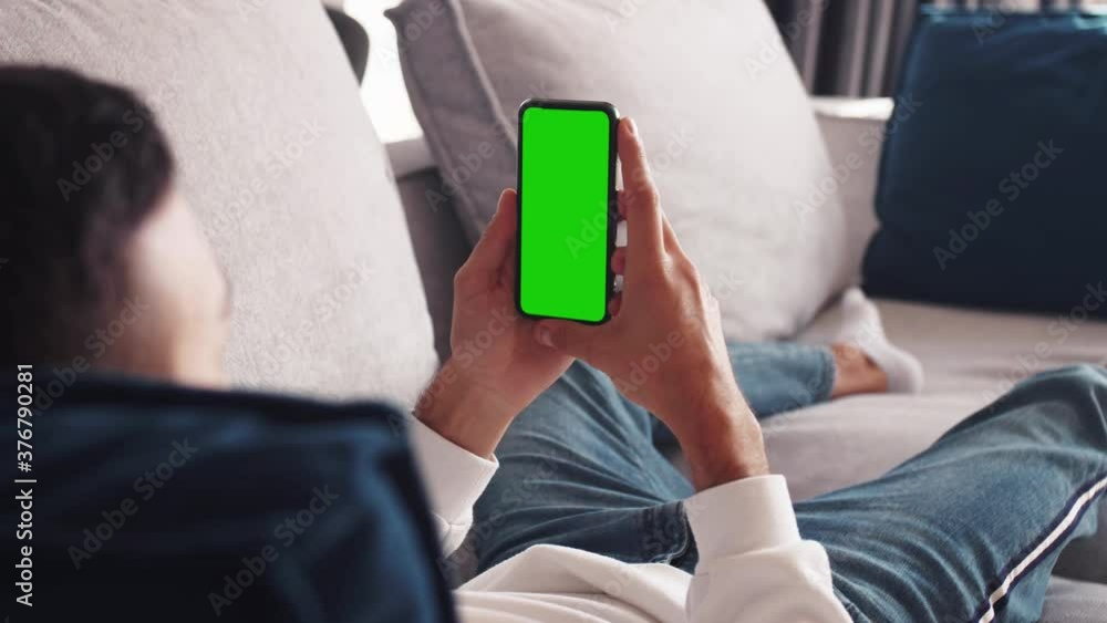Man lying on couch using smartphone with chroma key green screen , scrolling various gestures ...