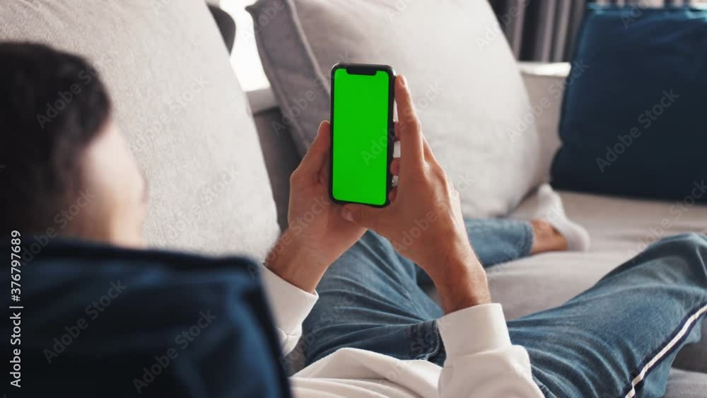 Man lying on couch using smartphone with chroma key green screen , scrolling various gestures ...