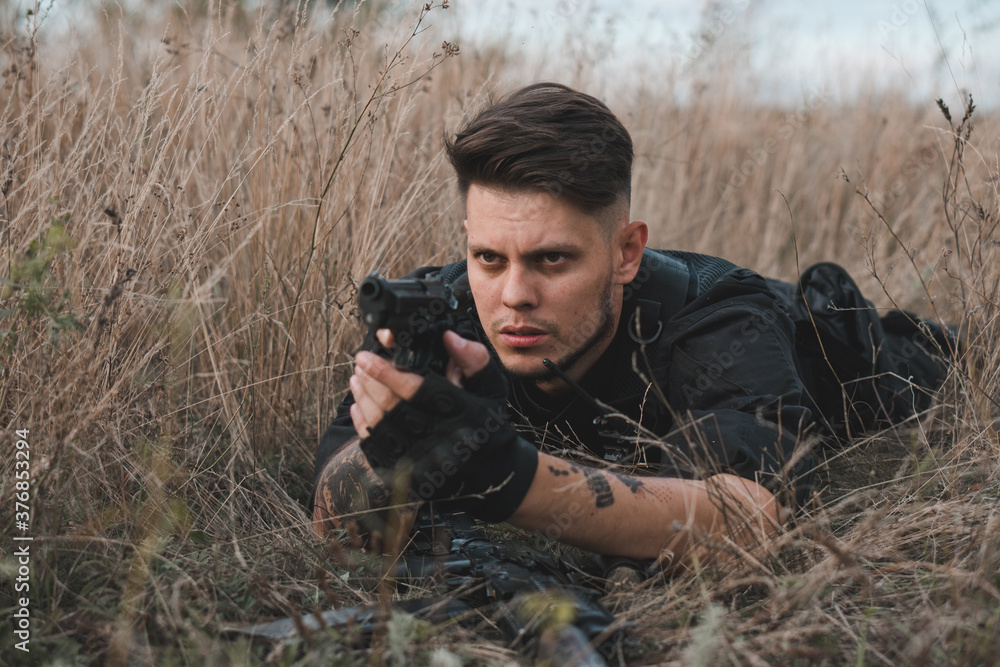 Young soldier in black uniform lying down and aiming a pistol. Stock ...