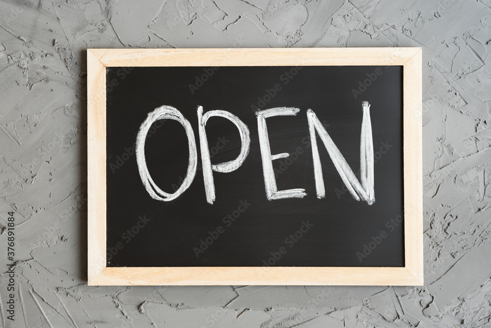 Word "Open" written on a blackboard, concrete wall as background. Open ...