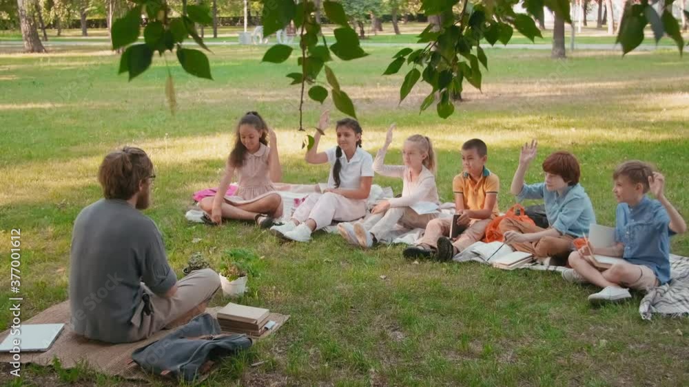 Medium shot of male elementary school teacher sitting cross-legged ...