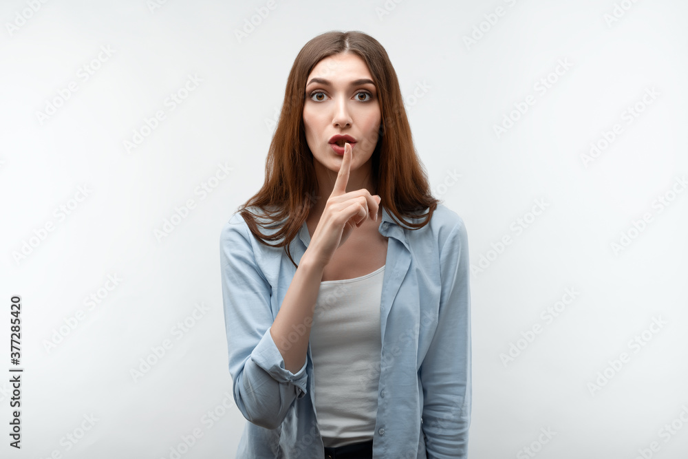 Pretty girl with long chestnut hair keeps finger on lips, making hush ...