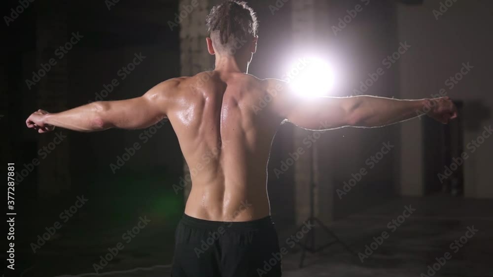 Strong bodybuilder posing backside after training with spotlight lens ...