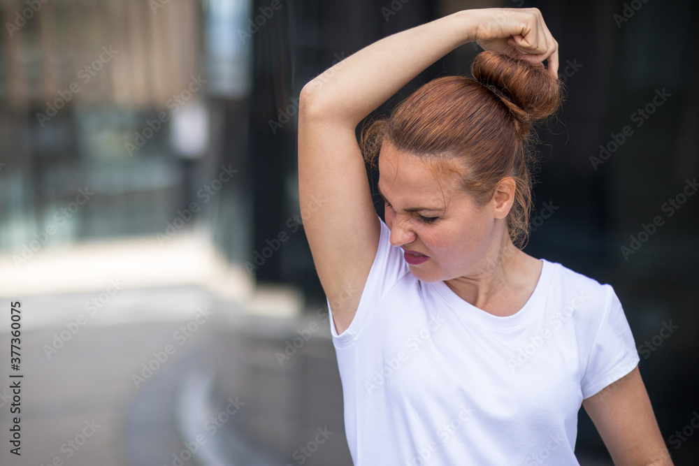 Sweaty girl sniffs her armpits in disgust in white T-shirt. Young woman ...