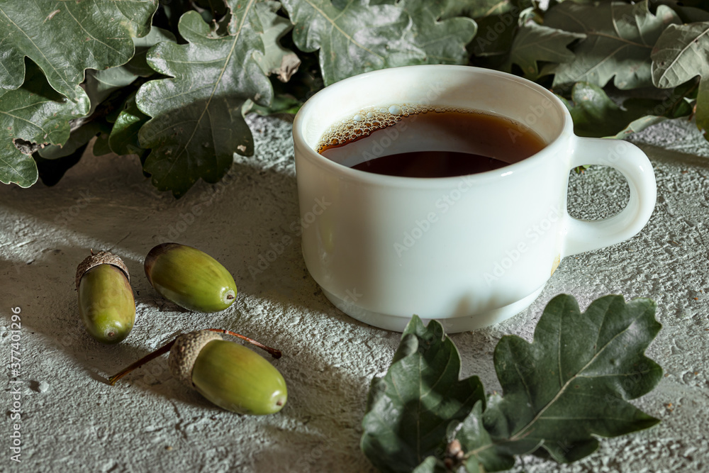 Cup of acorn coffee, acorns and green oak leaves on a gray background ...