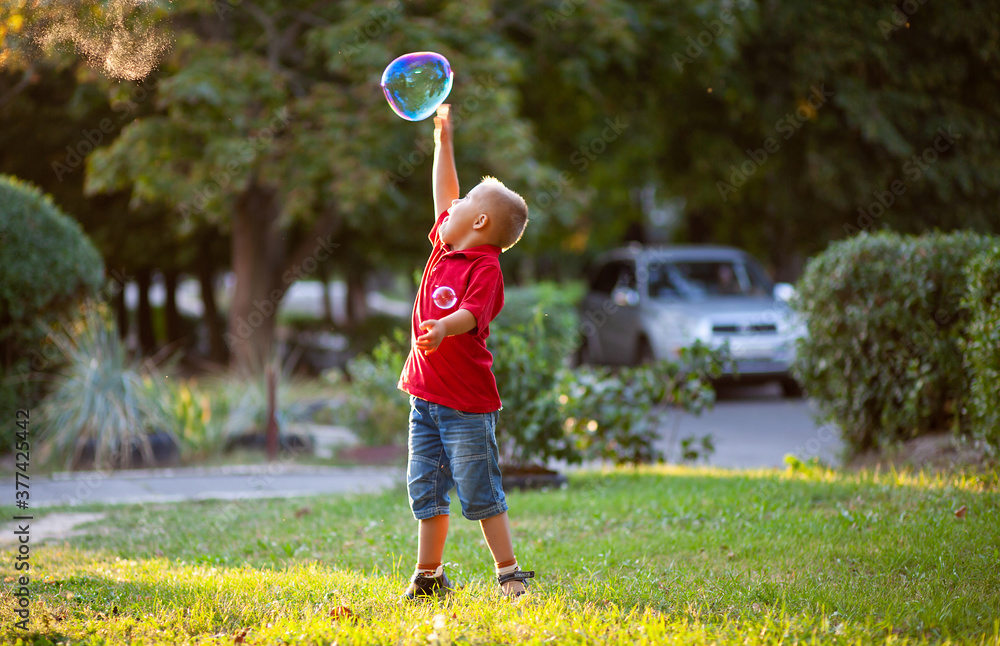 Little cute boy with Down Syndrome plays with huge soap bubbles in the ...