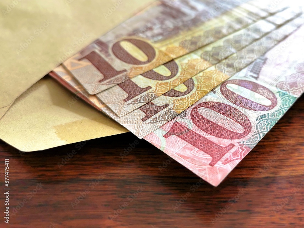 Hand pulling 10 Riyal and 100 Riyal Saudi banknotes from an envelope on ...