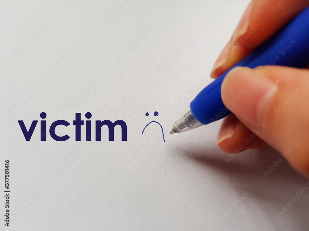 A hand drawing a sad face emoticon with the word victim written on a ...